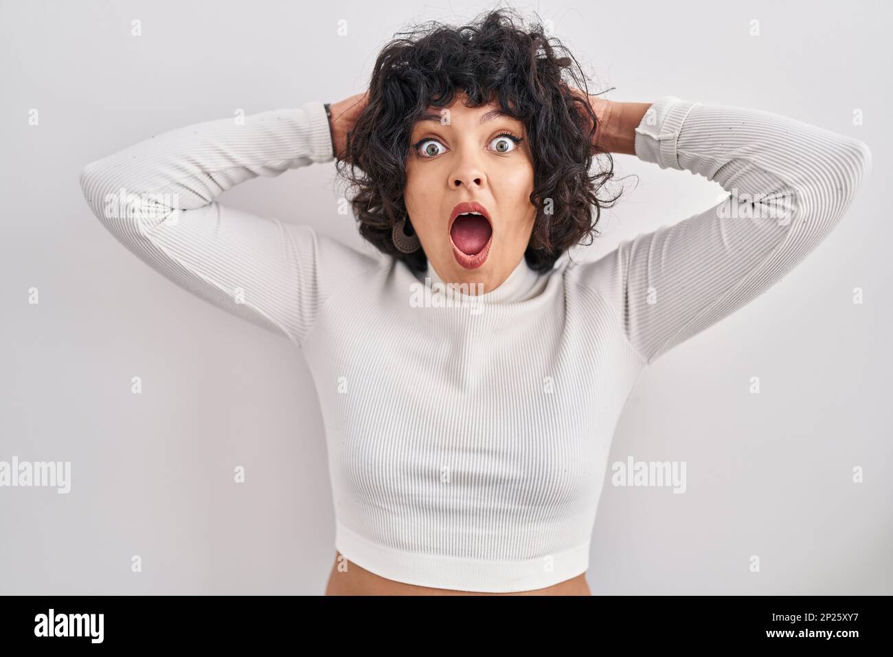 Hispanic woman with curly hair standing over isolated background crazy ...