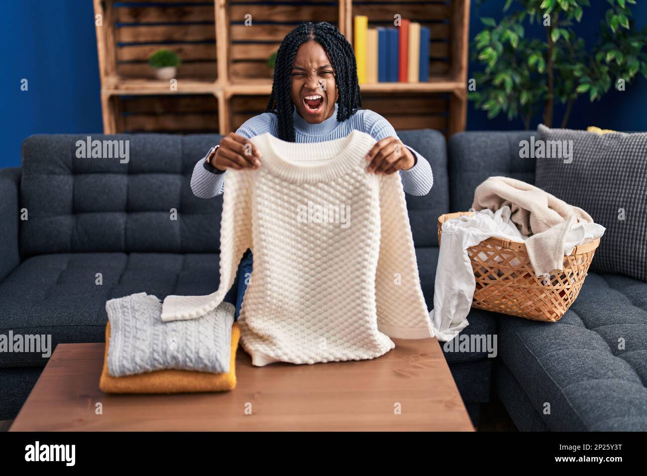 African american woman folding clean laundry angry and mad screaming ...