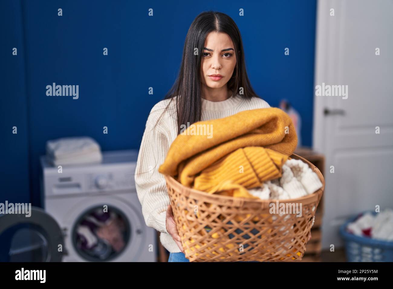 Young woman holding laundry basket depressed and worry for distress, crying angry and afraid ...
