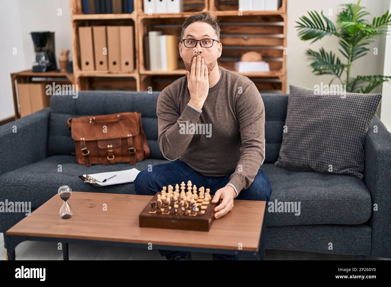 Middle age caucasian man playing chess sitting on the sofa covering ...