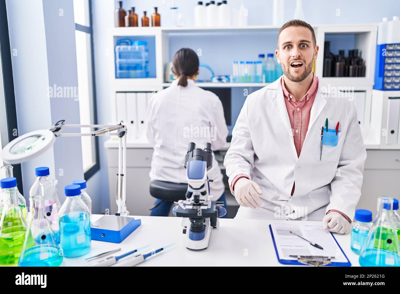 Young man working at scientist laboratory scared and amazed with open ...