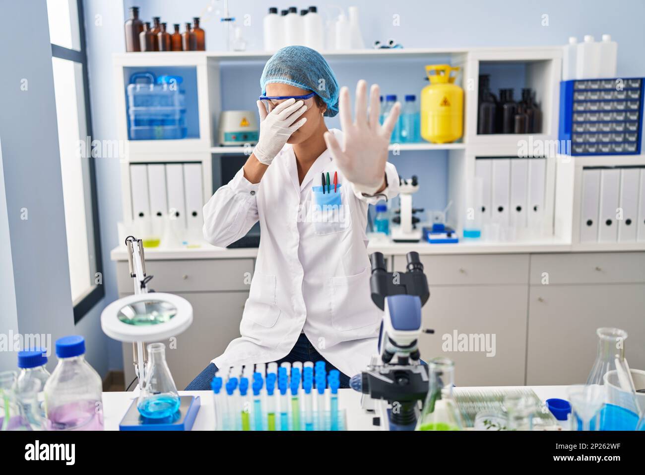 Brunette woman working at scientist laboratory covering eyes with hands ...