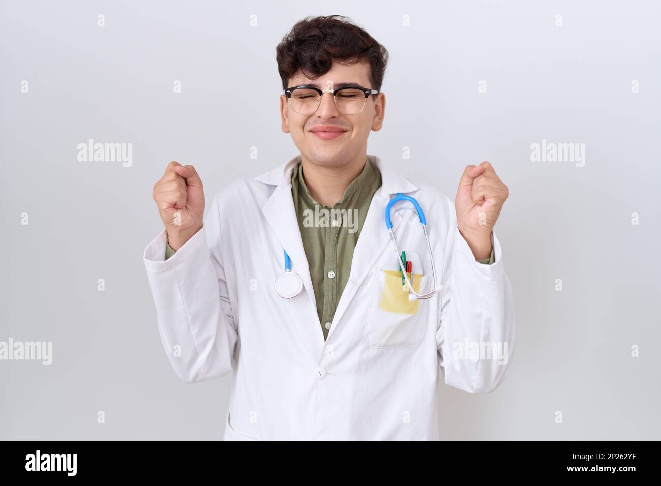 Young non binary man wearing doctor uniform and stethoscope excited for ...