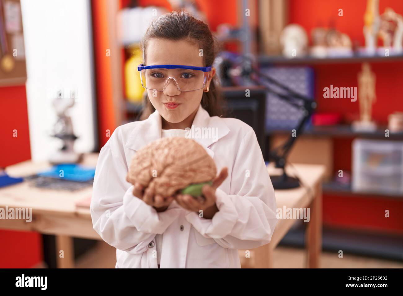 Little hispanic girl holding brain at science class at school puffing ...