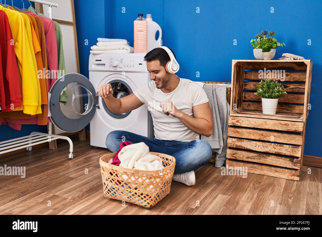 Young hispanic man dancing and listening to music washing clothes at ...