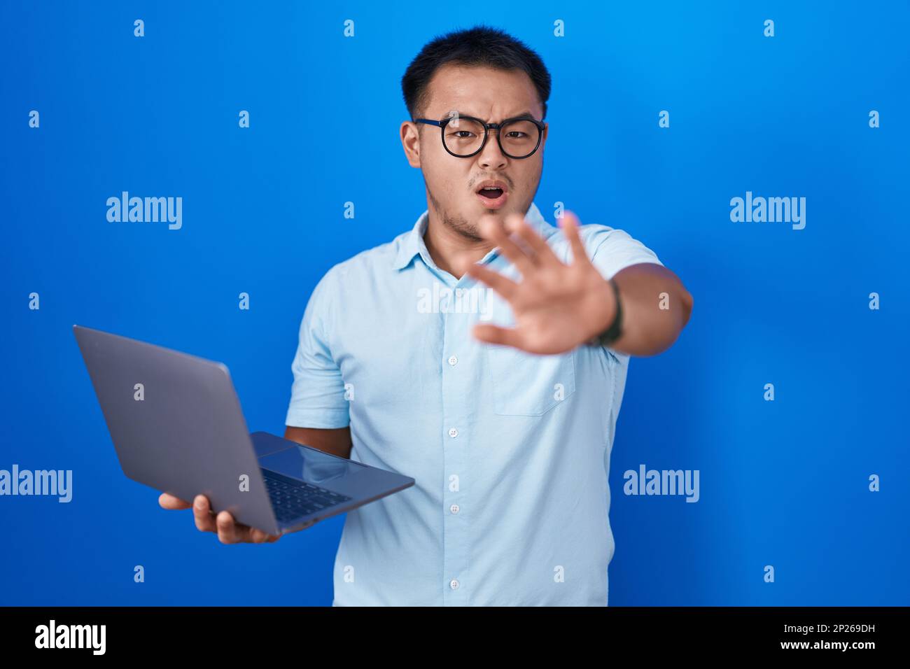 Chinese young man using computer laptop doing stop gesture with hands ...