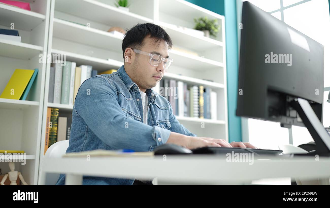 Young chinese man student using computer studying at library university ...