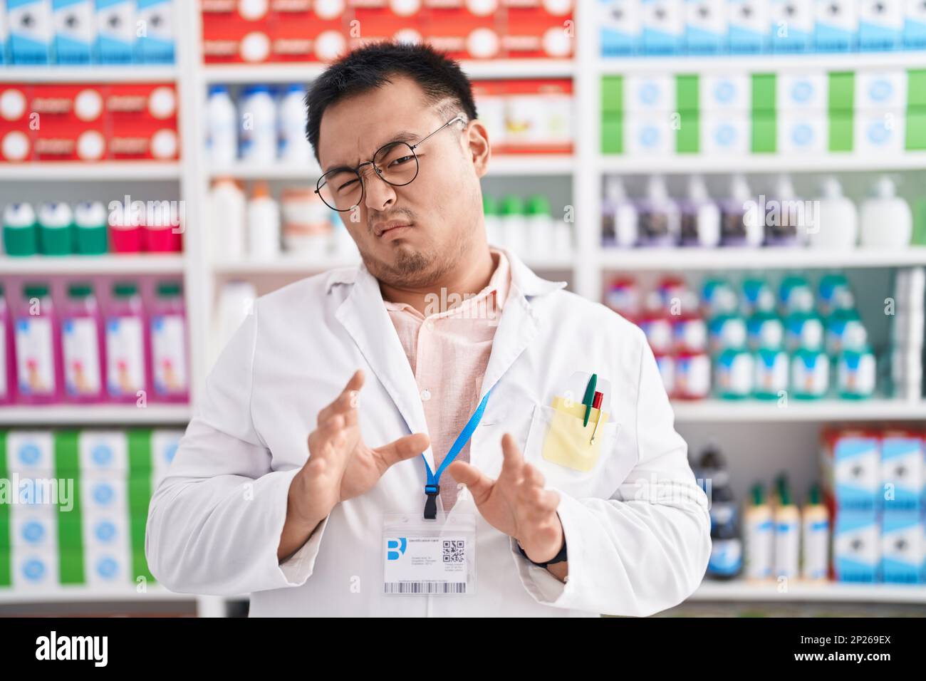 Chinese young man working at pharmacy drugstore disgusted expression ...