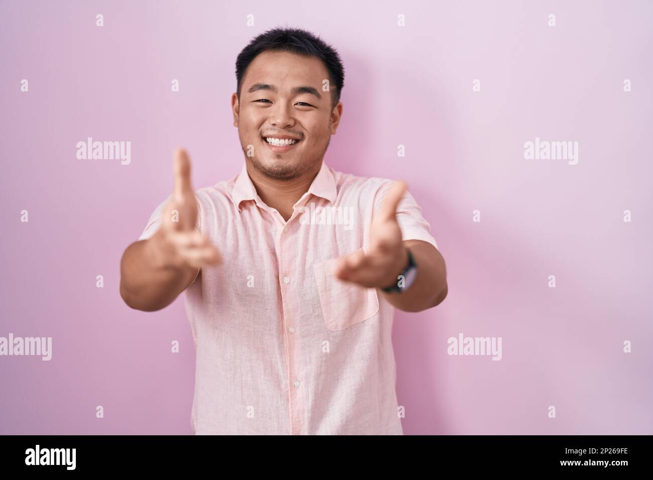 Chinese young man standing over pink background smiling cheerful ...