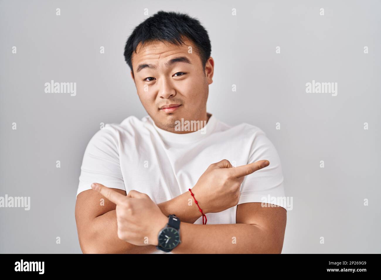 Young chinese man standing over white background pointing to both sides ...
