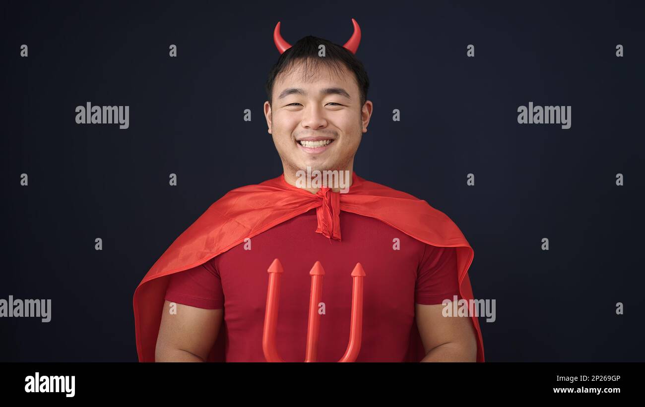 Young chinese man wearing devil costume holding trident over isolated ...