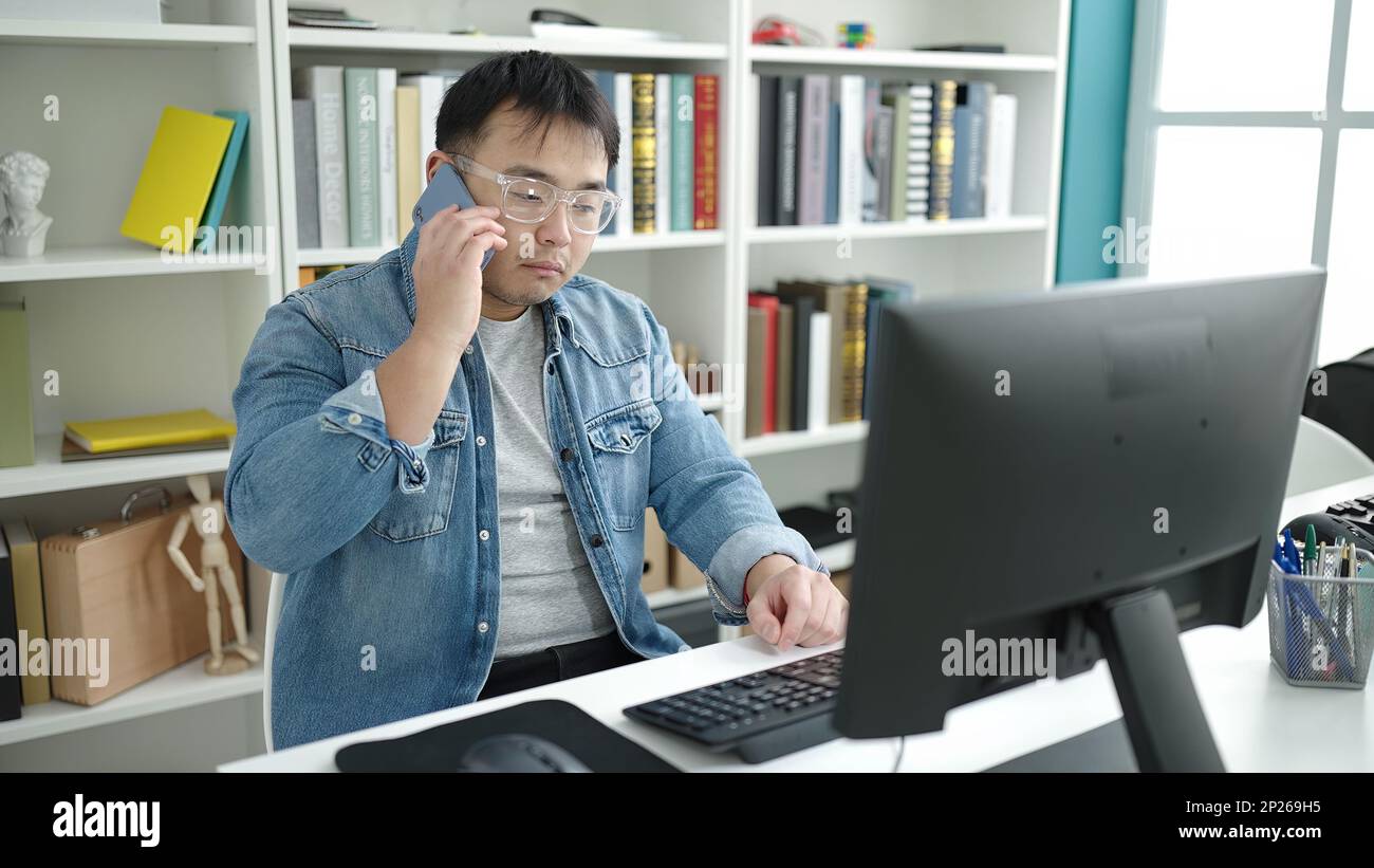 Young chinese man student using computer talking on smartphone at ...