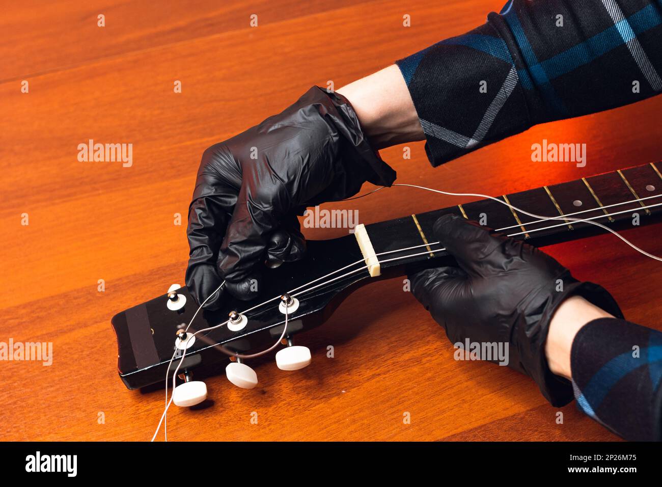 man with guitar,master hands in gloves puts on new strings and tuning ...