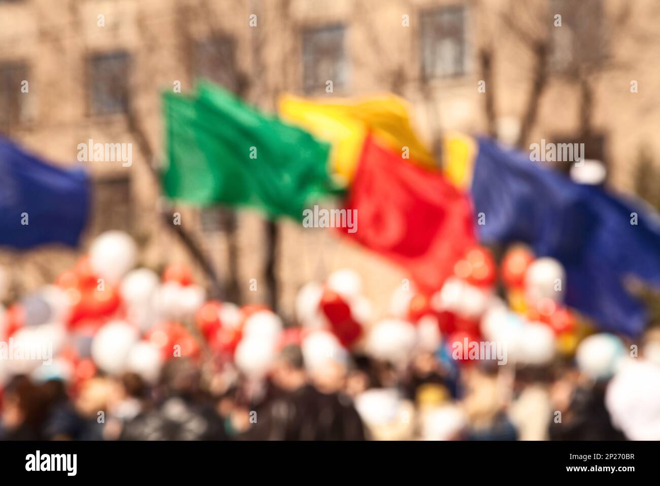 Crowd of people on a May Day march carrying colorful balloons and flags ...