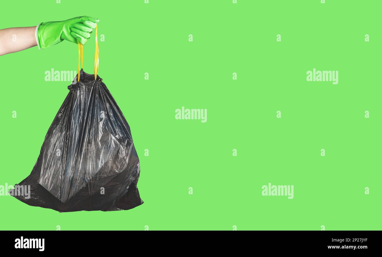 Hand in glove holding handles of black plastic disposable trash bag ...