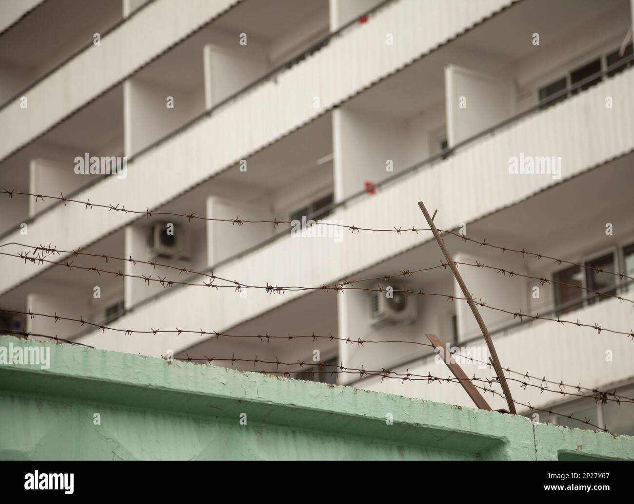 White residential building behind the concrete fence with barbed wire ...