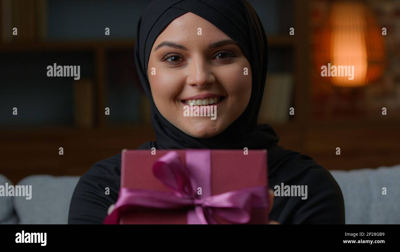 Smiling woman in hijab hold pink gift box with ribbon wishing happy ...
