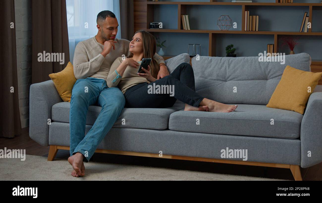 Millennial 30s couple rest on sofa using mobile phone make remote ...