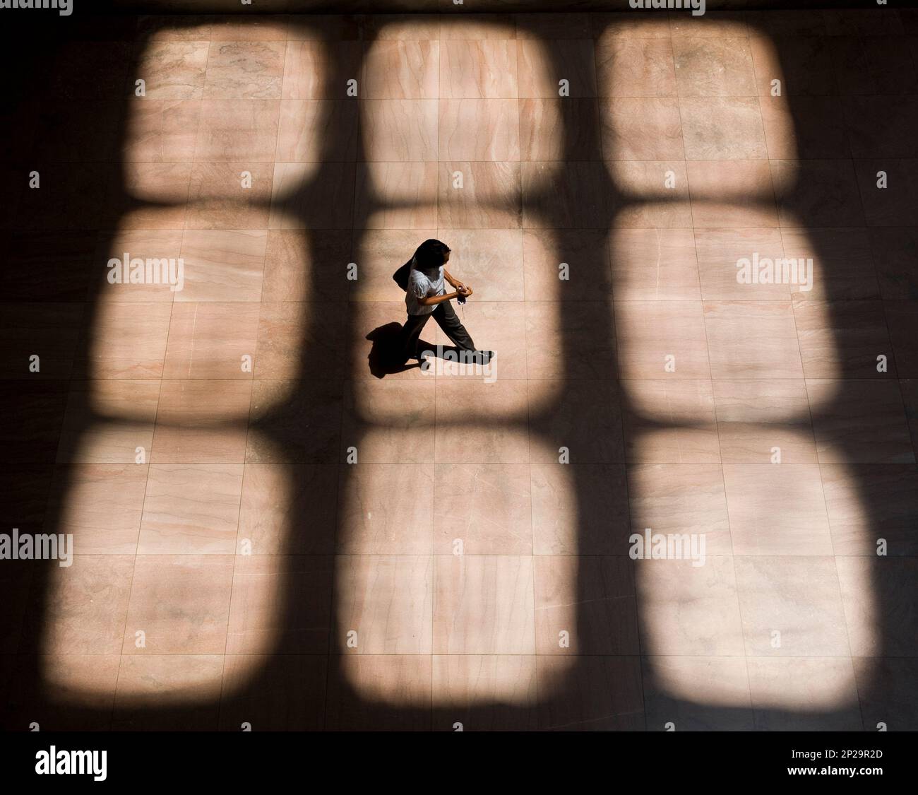 A woman walks through shafts of light shining down on the atrium of the ...
