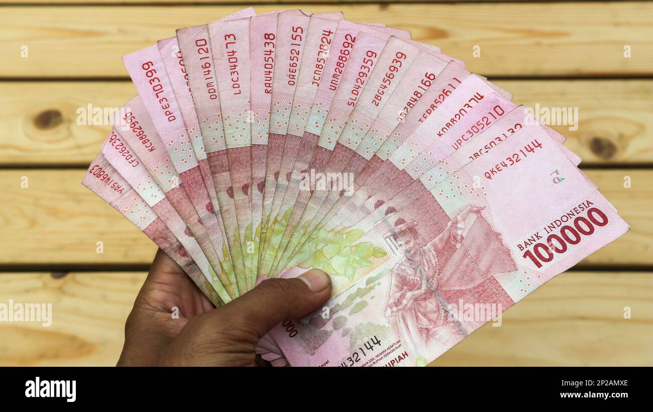 A man's hand holds a hundred thousand rupiah note. Indonesian rupiah ...