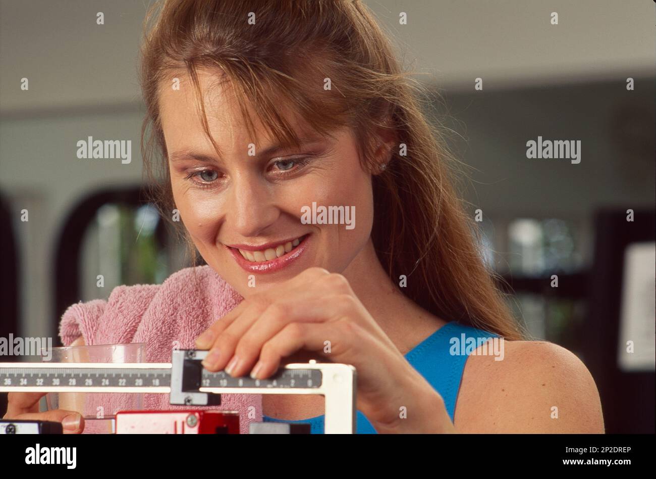 Young woman at a gym standing on a scale weighing herself liking the ...