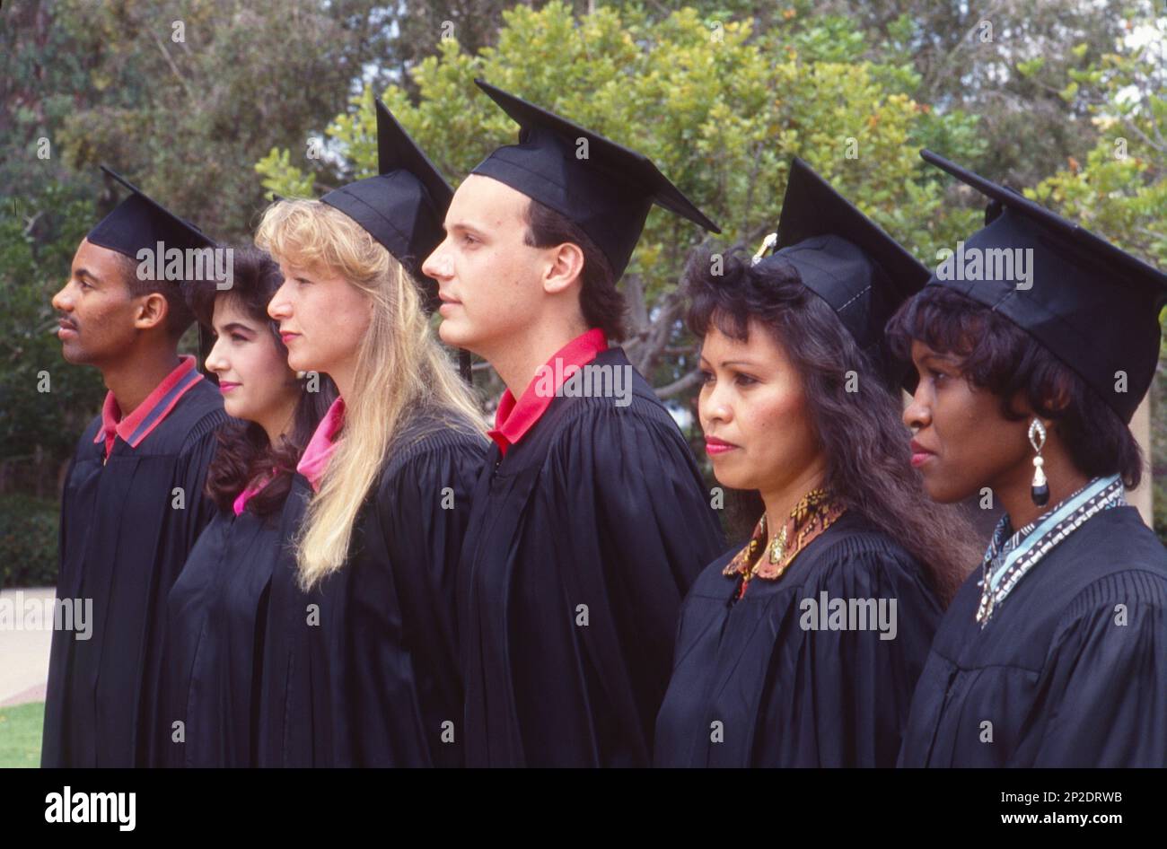 Row of teenagers, boys and girls in their cap & gowns at graduation ...