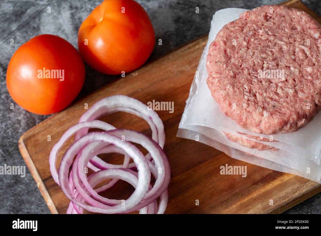 Raw beef burgers stacked on a wood cutting board, separated with ...