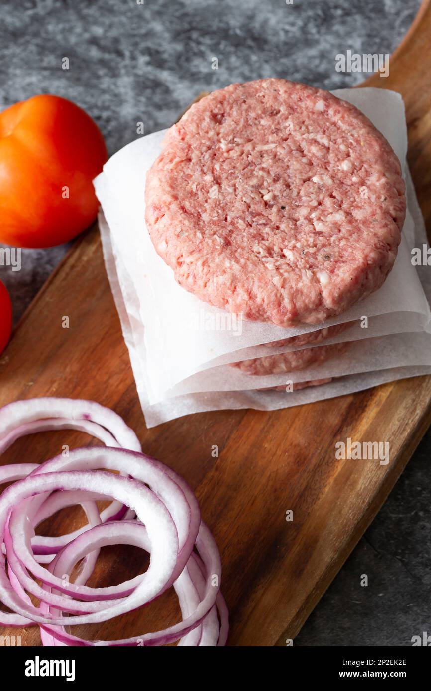 Raw beef burgers stacked on a wood cutting board, separated with ...