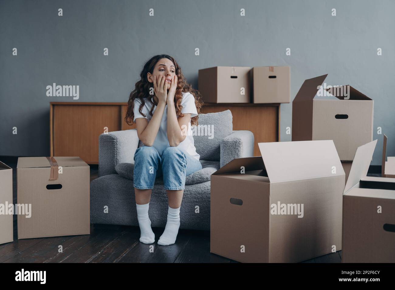 Tired young woman sitting near cardboard boxes on relocation day ...