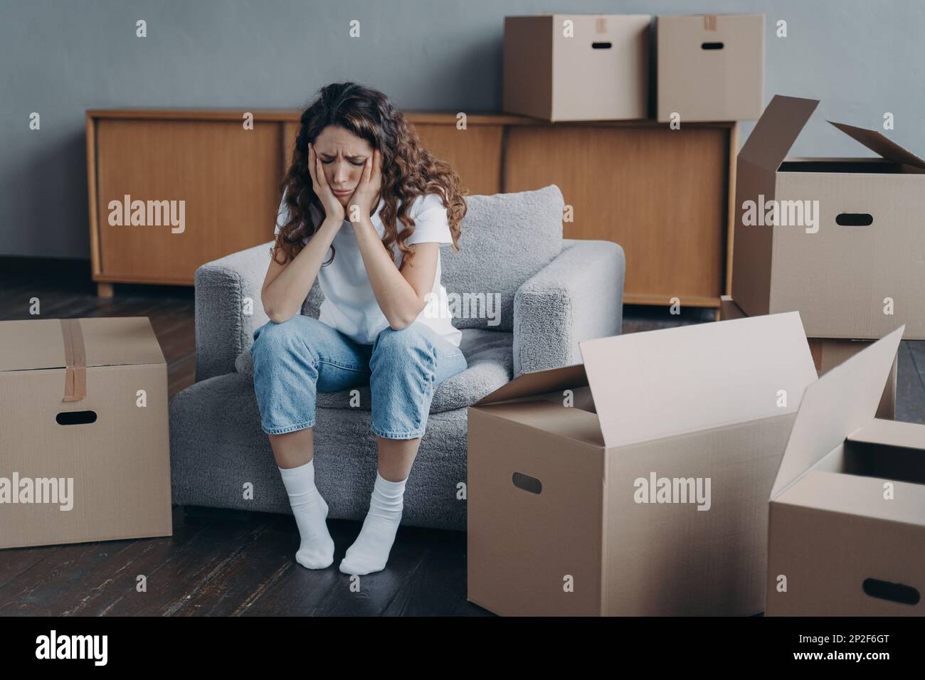 Exhausted upset young spanish woman tenant sitting on armchair in empty ...