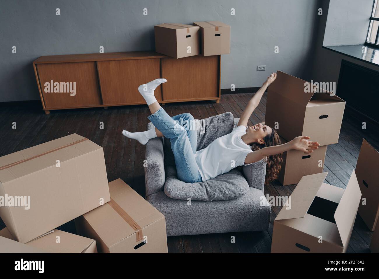 Joyful female homeowner having fun in armchair lifting hands celebrates ...