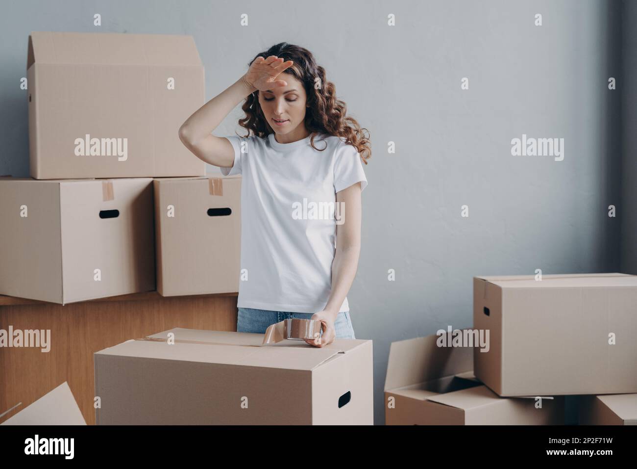 Tired woman packing cardboard boxes with things, using adhesive tape ...