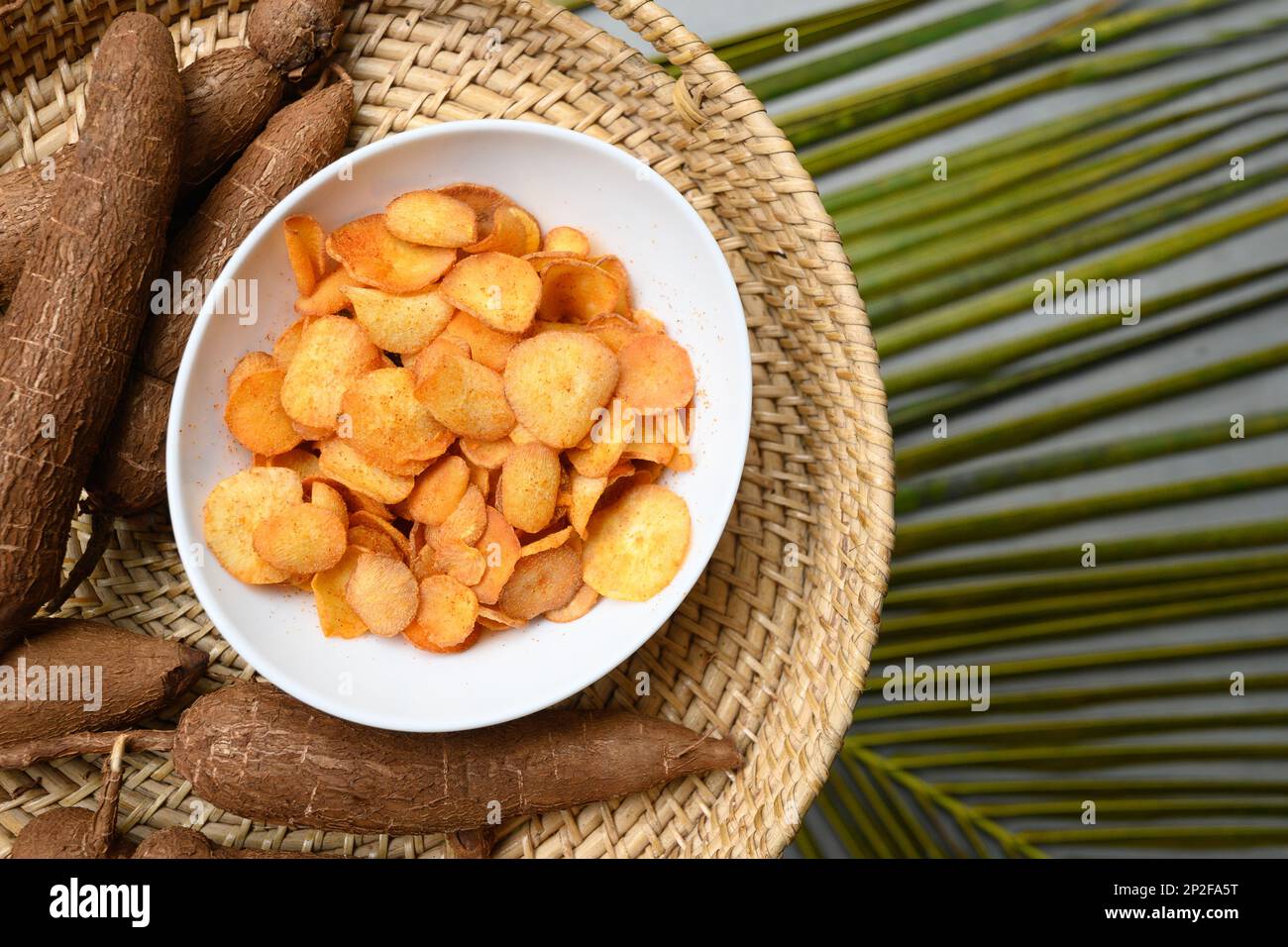 Organic yuca or cassava chips in bowl and tapioca root on palm leaves ...