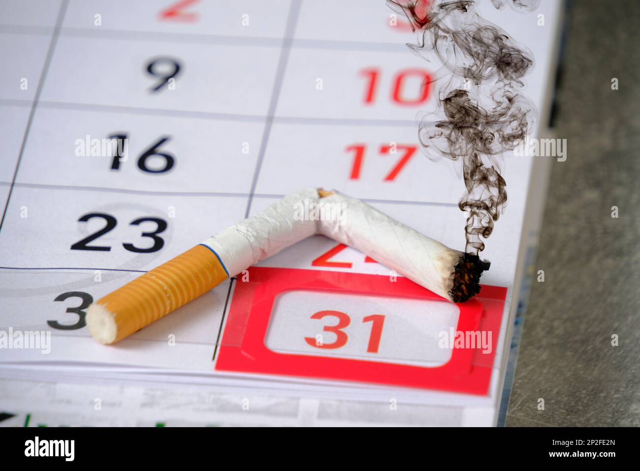 Black smoke coming from discarded cigarette.Background is calendar with ...