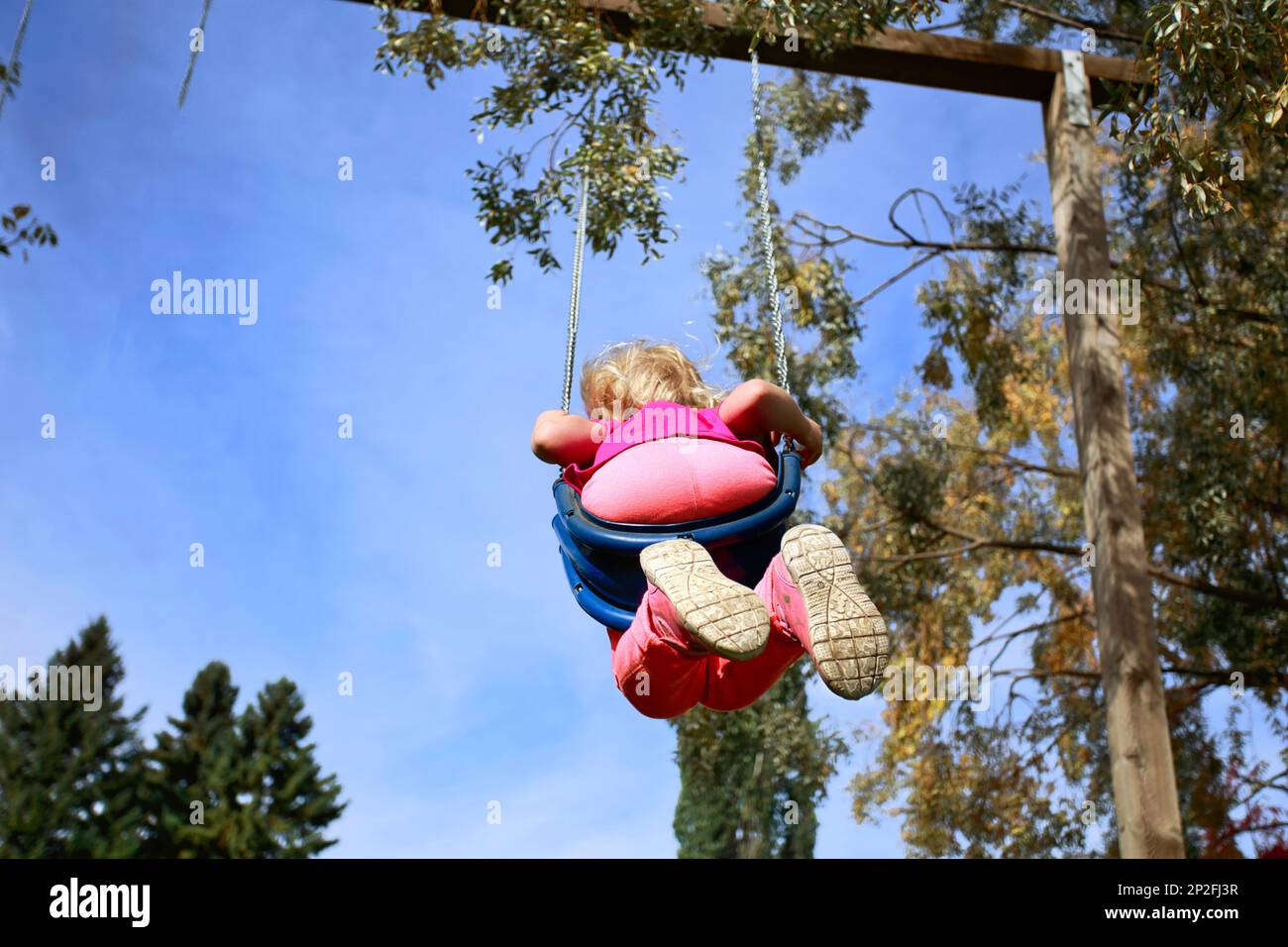 the backside of a little girl in pink clothes swinging up in the air on ...