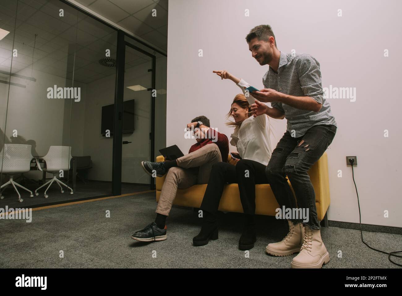 Lovely coworkers having fun and dancing while sitting on a sofa at the ...