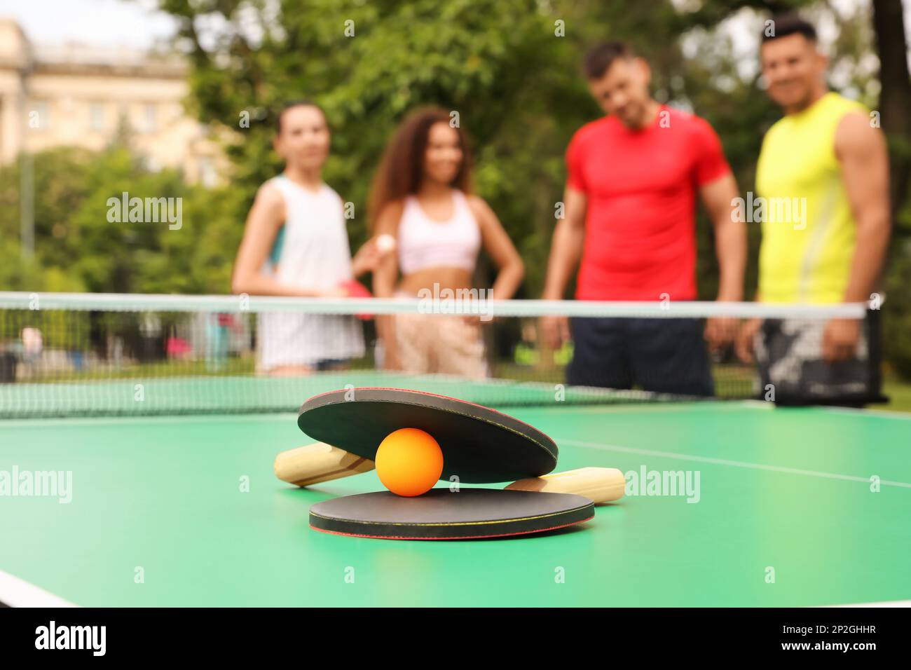 Friends talking near ping pong table outdoors, focus on rackets and ...