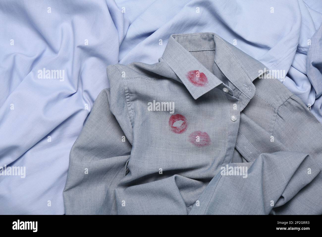 Men's shirt with lipstick kiss mark among other clothes as background ...