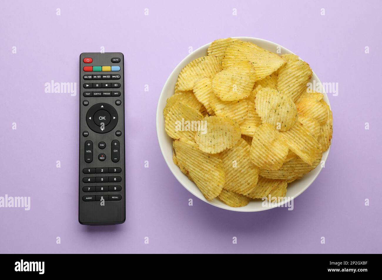 Remote control and bowl of potato chips on violet background, flat lay ...