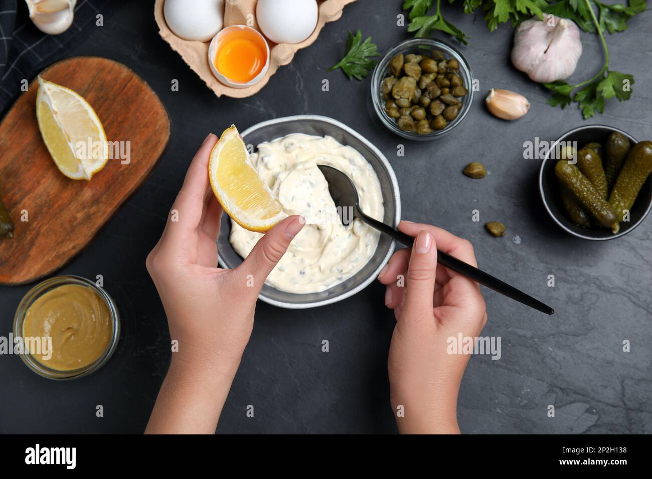 Woman adding lemon juice to tartar sauce at black table, top view Stock ...
