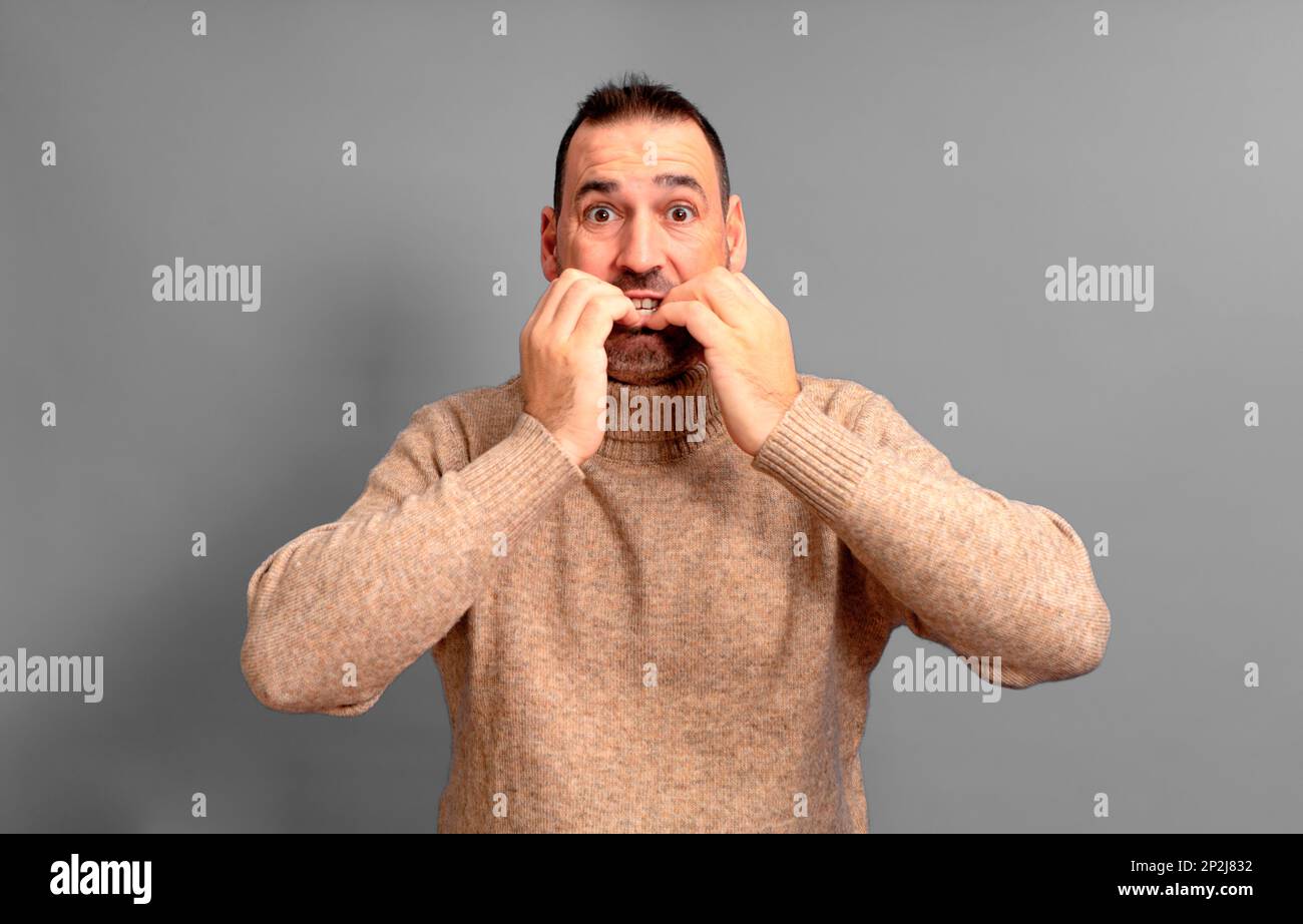 Hispanic man in his 40s scared and shocked biting his nails, staring ...