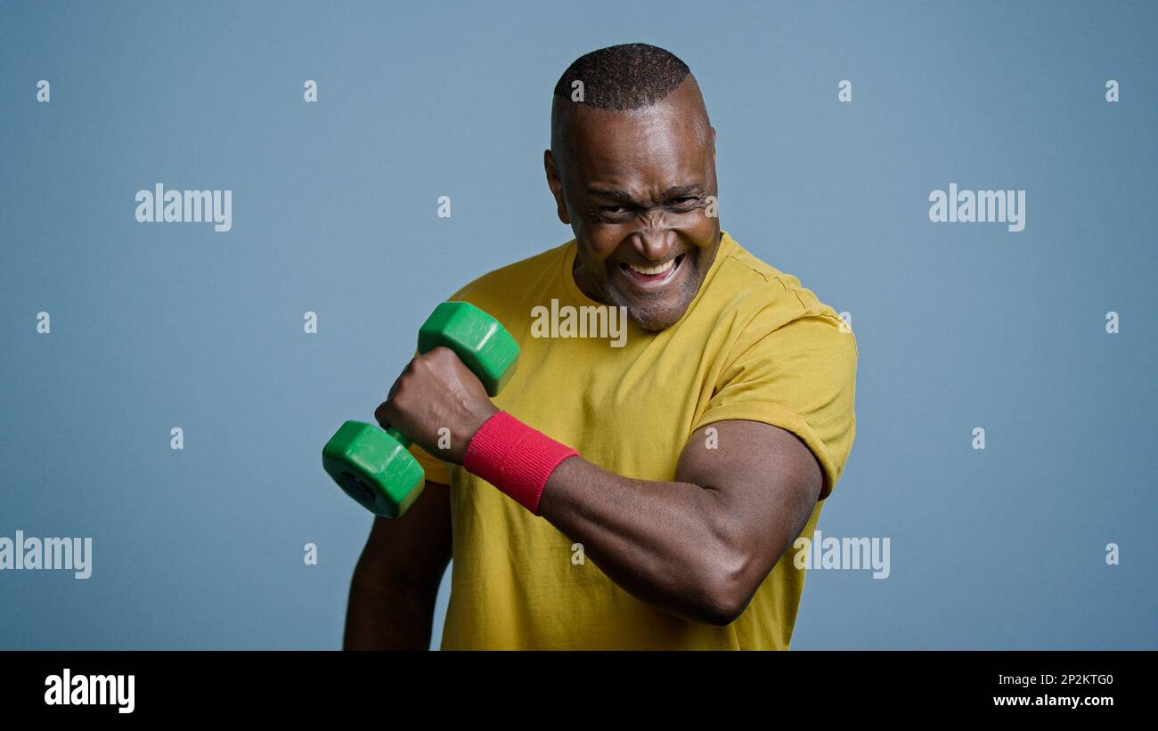 Mature strong athletic man coach pumping biceps with dumbbell in studio ...