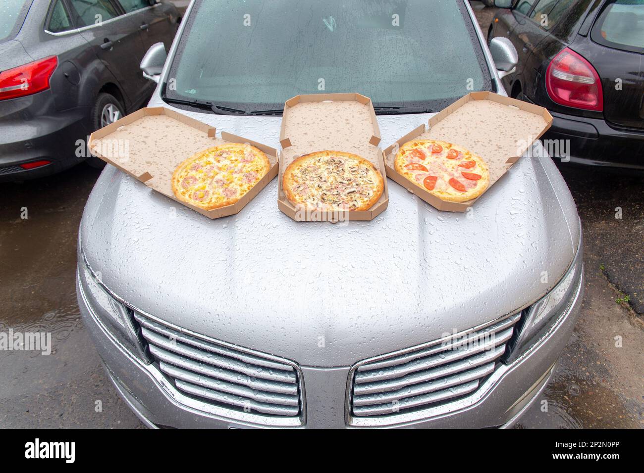 Three pizzas in open cardboard takeaway boxes are lying on the hood of ...