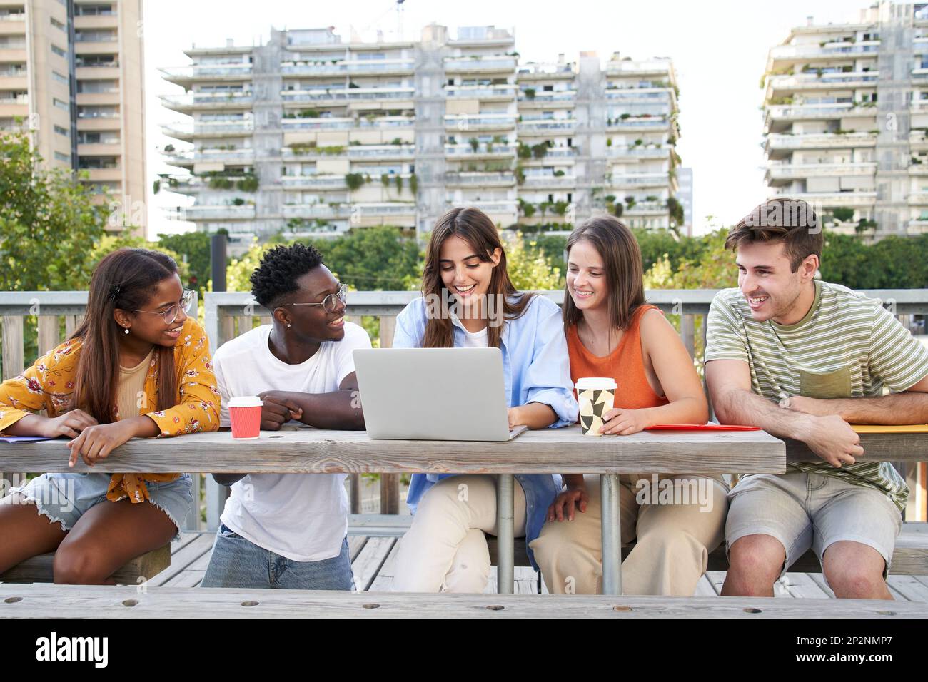 Group of cheerful multiracial students together happily looking at laptop outdoors. Portrait ...