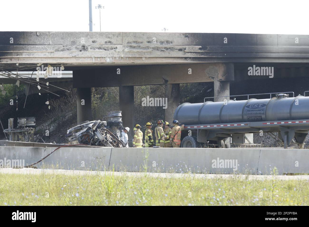 Fire officials stand by an overturned tanker truck that caught fire ...