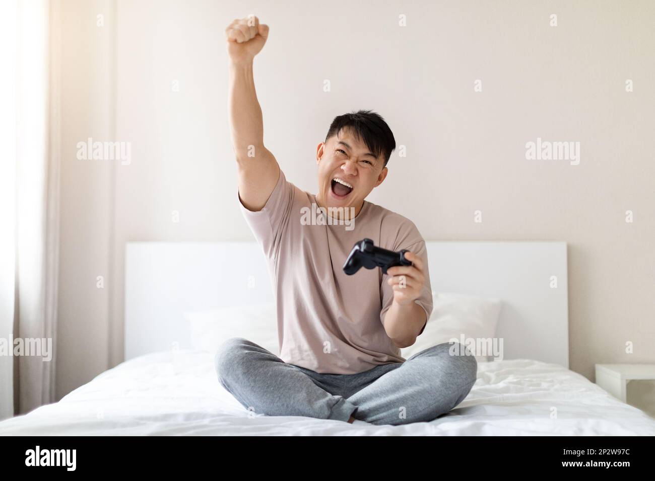 Happy emotional asian man playing video games at home Stock Photo - Alamy