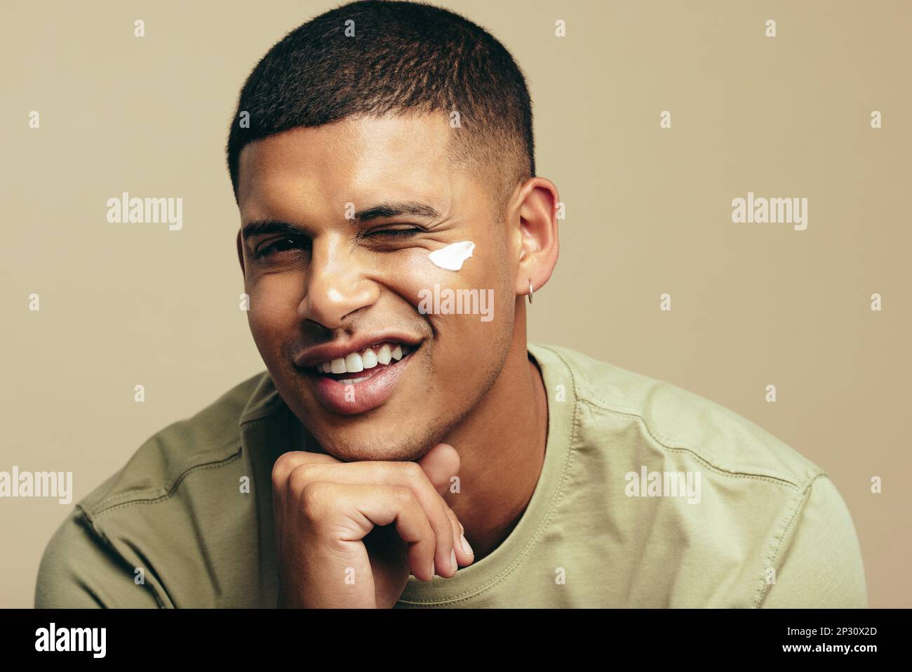 Handsome young having fun while taking care of his skin, he smiles and ...