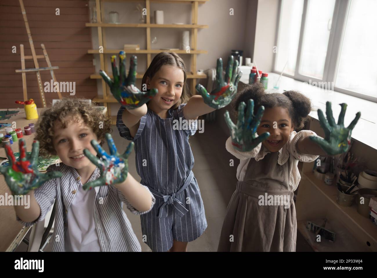 Cheerful multiethnic kids posing at camera in creative craft studio ...