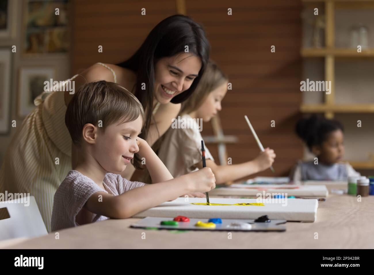 Cheerful pretty teacher girl helping pupil boy with drawing picture ...