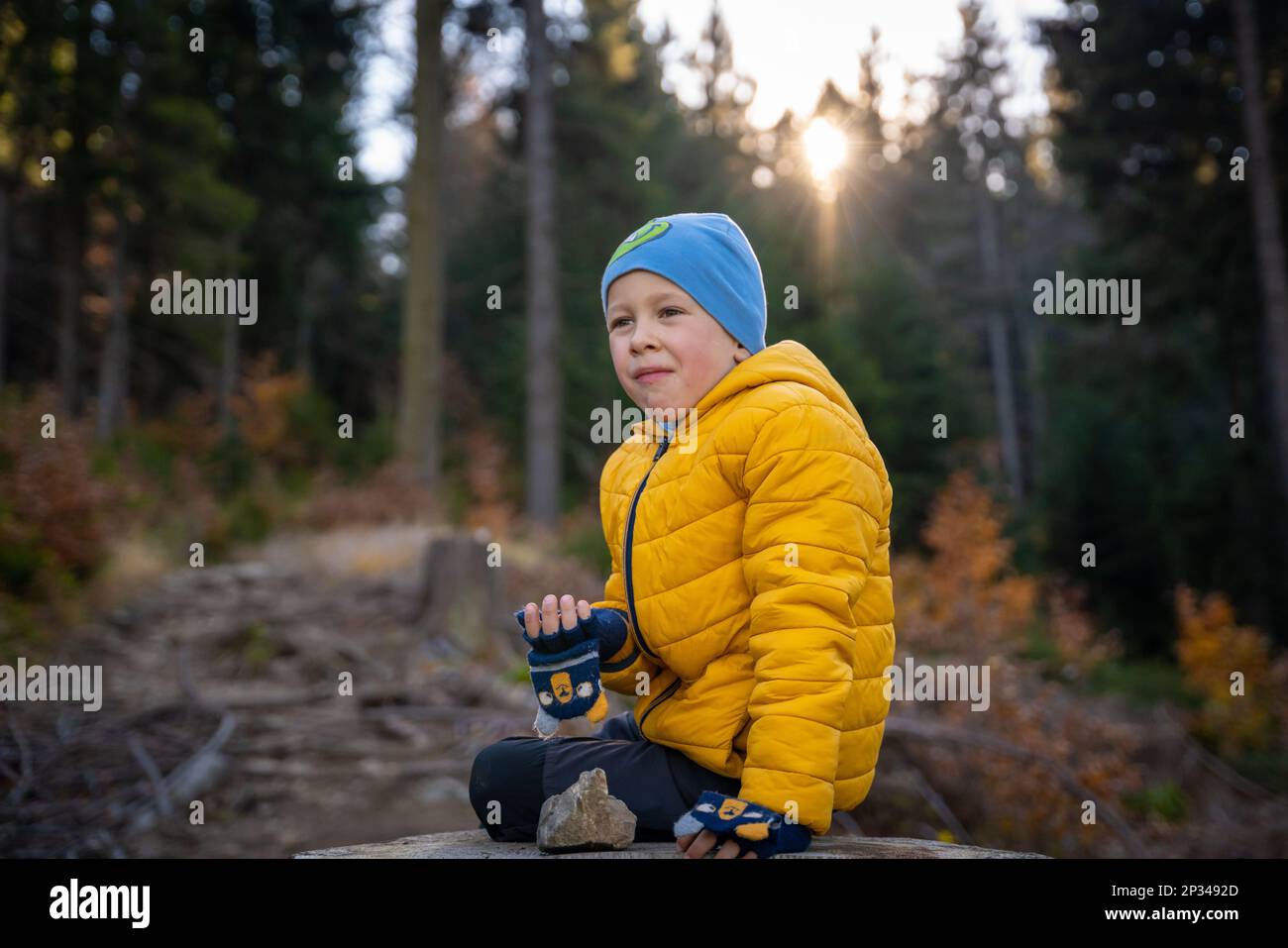Little kid is sitting on a big stump on the mountain trail, eating ...